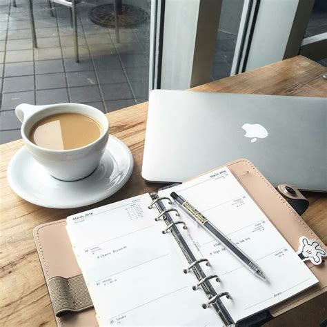 A Cup Of Coffee Sitting On Top Of A Wooden Table Next To A Laptop Computer