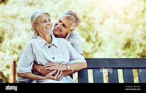 Love Nature And Elderly Couple Hugging While Sitting On An Outdoor Bench In The Park Happy