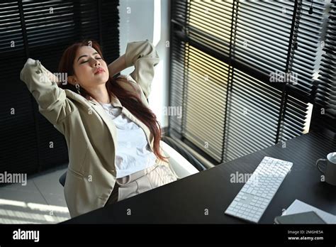 Relaxed Businesswoman Sitting Back In Her Office Chair With Closed Eyes And Hands Clasped Behind