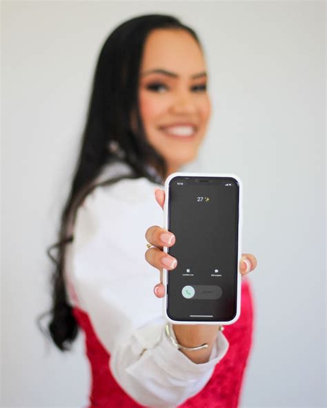 A Woman Holding Up A Cell Phone In Front Of Her Face And Smiling At The
