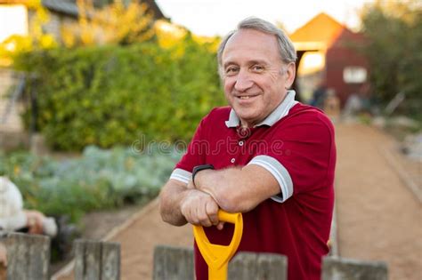 Mature Man Standing Relaxed Near Fence With Shovel In Backyard Smiling