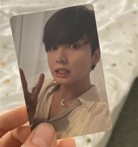 A Person Holding Up A Polaroid Photo In Front Of A Bed With White Sheets