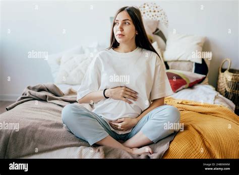 Pregnant Caucasian Brunette Expectant Mom Sitting On The Bed Holding