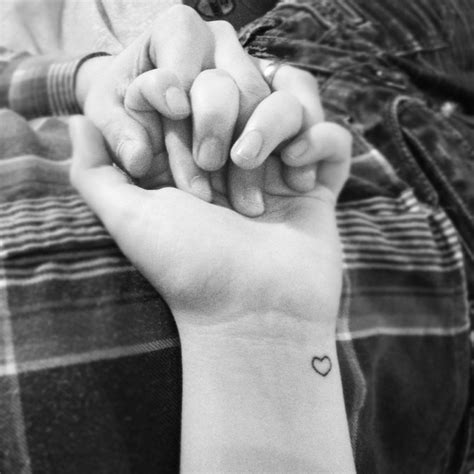 Two Hands Holding Each Other With A Small Heart Tattoo On The Wrist