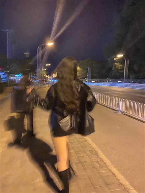 Two People Walking Down The Street At Night With Their Backs Turned To