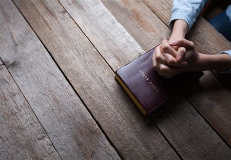 Hands Praying With A Bible In A Dark Over Wooden Table Gospel