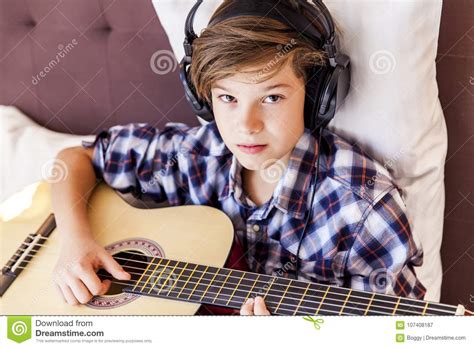 Adolescente Que Toca La Guitarra Acústica En Cama Imagen de archivo
