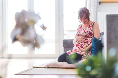 Happy Pregnant Mother Is Sitting On The Floor Hugging Her Tummy Stock