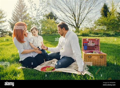 Beautiful And Stylish Redhead Mom In A White Blouse Sits On The Grass With Her Beautiful Man