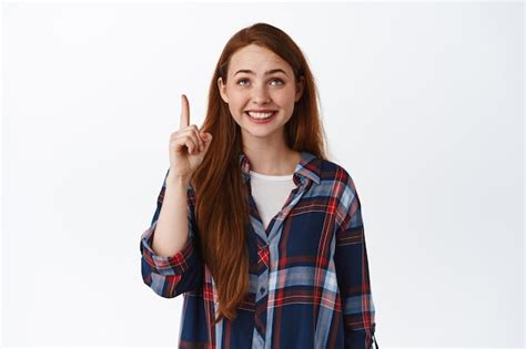 陽気な十代の赤毛の女の子笑顔とポンティング見上げて白い背景に立って驚いた幸せそうな顔でトップのロゴを見つめて プレミアム写真