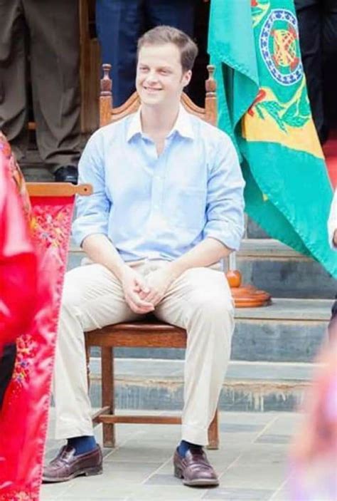 A Man Is Sitting On A Chair In Front Of Other People And Flags Smiling
