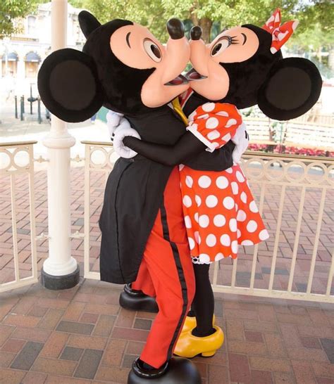 Mickey And Minnie Kissing Each Other In Front Of A White Fence