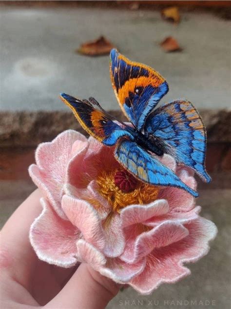 Two Butterflies Sitting On Top Of A Pink Flower In Someone S Hand With
