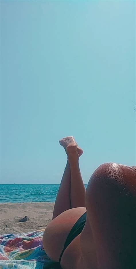 A Woman Laying On Top Of A Beach Next To The Ocean Under A Blue Sky