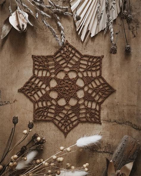 An Intricate Doily On The Side Of A Wall Next To Dried Plants And Feathers
