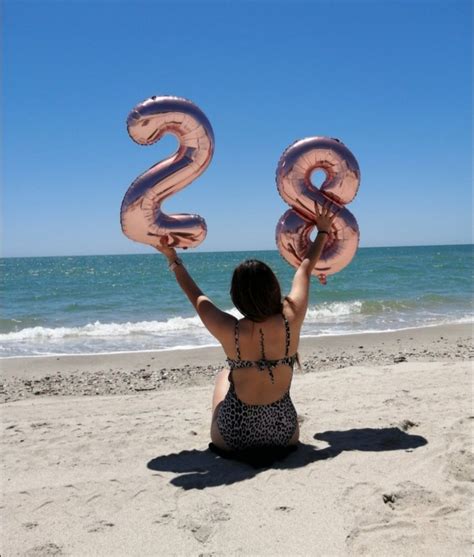 A Woman Sitting On The Beach Holding Up Two Large Balloons In The Shape