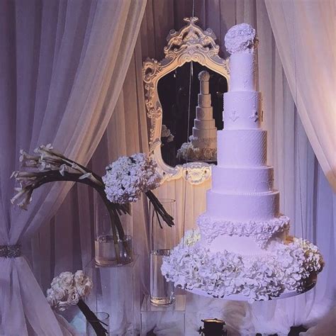 A Large Wedding Cake Sitting On Top Of A Table Next To A Mirror And Flowers