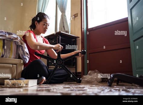 Side View Of Ethnic Asian Female Screwing Wheels To Chair Base While Sitting Cross Legged On