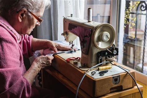 Vieja abuela cosiendo ropa a máquina frente a la ventana Foto Premium