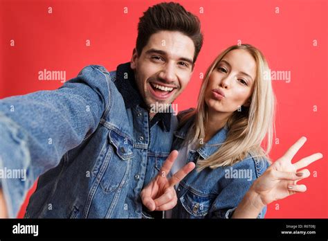 Portrait Of A Smiling Young Couple Dressed In Denim Jackets Standing Together Isolated Over Red