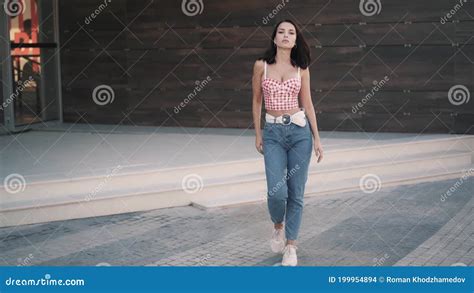 Woman Model In Red Top And Jeans Is Walking Forward Towards The Camera