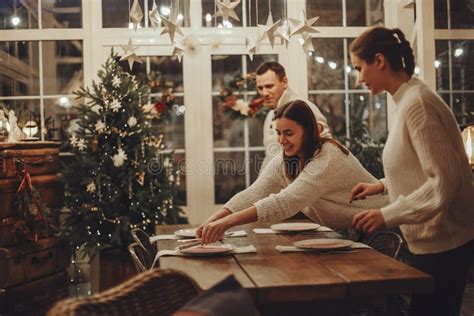 Mother Father And Daughter Setting Festive Christmas Table Together At Cozy Decorated Rustic