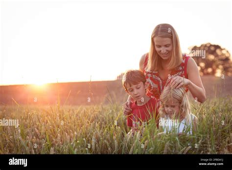 Boy And Girl Looking At Plants In Front Of Mother On Agricultural Field