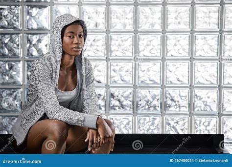 Black Woman With Elbows Leaning On Knees Sitting On A Bench Stock Photo