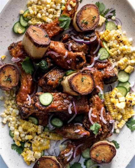 A White Plate Topped With Meat And Veggies On Top Of A Bed Of Corn