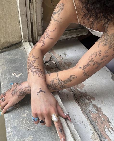 A Woman With Many Tattoos On Her Arm And Hand Leaning Against A Window
