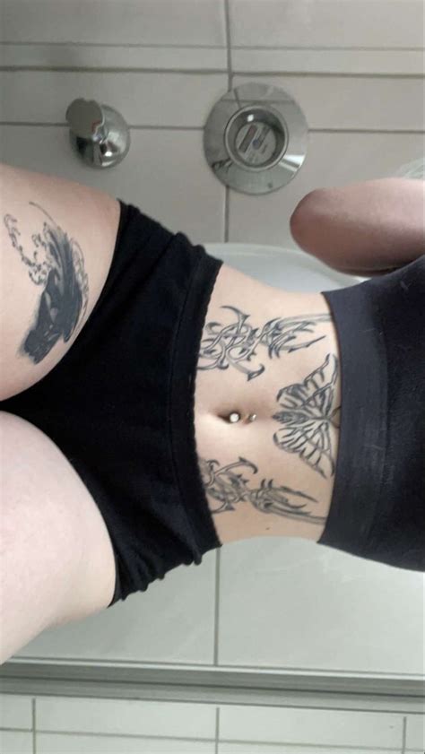 A Person With Tattoos On Their Legs Standing In Front Of A Bathroom