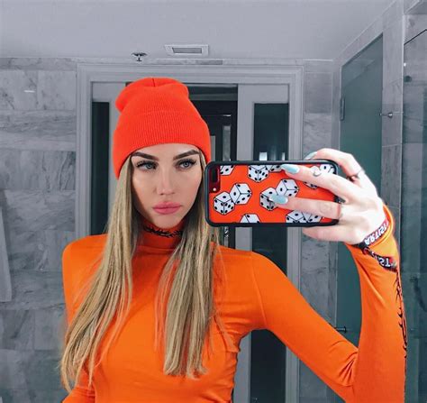 A Woman Taking A Selfie With Her Cell Phone Wearing An Orange Top And Hat