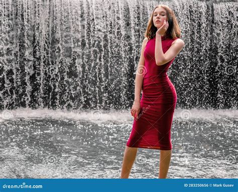 Teen Ager Girl In High Fashion Red Dress Posing In Water Water Fall Behind Her Back Prom
