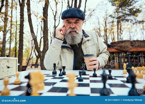 Portrait Of Thoughtful Senior Man Playing Chess In The Park On A