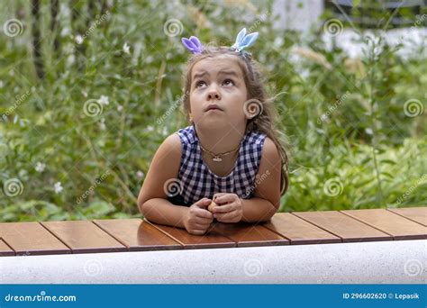 A Blonde 5 Year Old Girl Looks Up Pensively Against A Backdrop Of Greenery And Nature Stock
