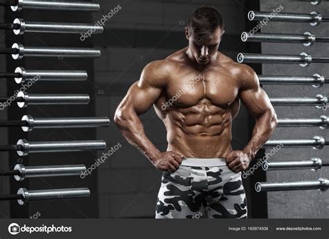 Hombre musculoso mostrando músculos posando en el gimnasio Fuertes