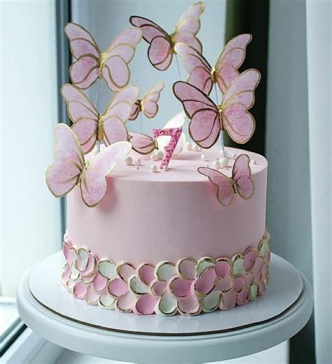 A Pink Cake With Gold Butterflies On It Sitting In Front Of A Window Sill