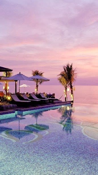 An Outdoor Swimming Pool With Lounge Chairs And Umbrellas At Dusk