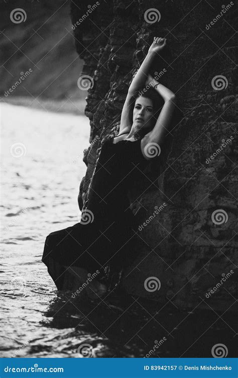 Seductive Girl In The Black Dress Standing Leaning Against The Rock