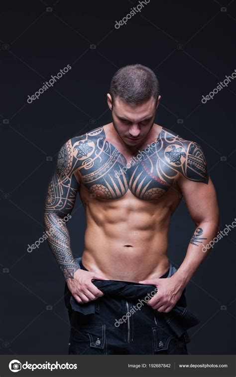 The Man With A Muscular Naked Torso With Tattoos On The Dark Background
