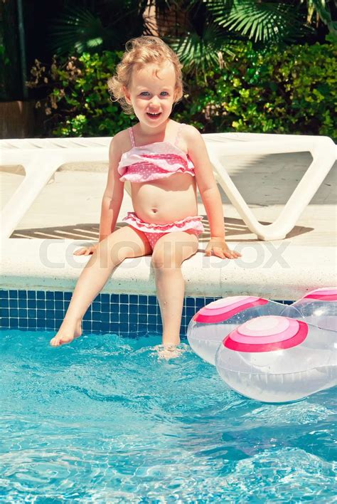 niedliche kleine Mädchen sitzt neben dem Schwimmbad Stock Bild