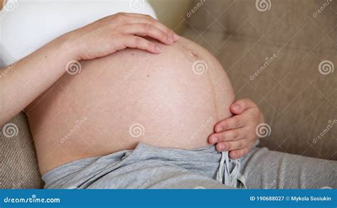 A Caring Mother Strokes A Naked Pregnant Tummy With Two Hands On Light