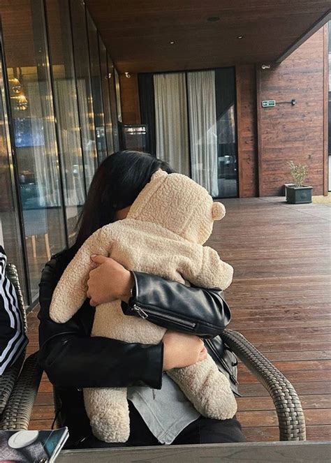 A Woman Sitting On A Bench Holding A Teddy Bear In Her Arms And Looking