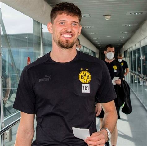 A Man Wearing A Face Mask And Black T Shirt Smiles At The Camera As
