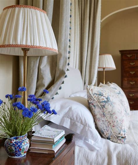 A Bed With White Sheets And Blue Flowers In A Vase Next To A Lamp On A