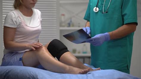 Physician Explaining Broken Leg Bone X Ray To Female In Neoprene Knee
