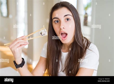 Beautiful Young Woman Eating Asian Sushi Using Chopsticks Scared In Shock With A Surprise Face