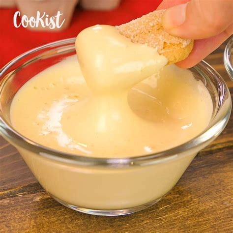 A Person Dipping Cheese Into A Small Glass Bowl