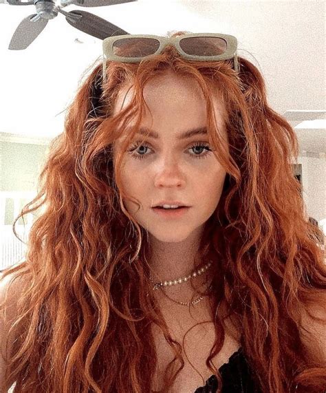 A Woman With Long Red Hair And Sunglasses On Her Head Is Looking At The Camera