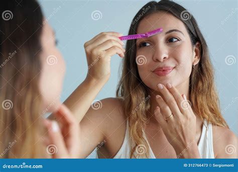 Dermaplaning Beautiful Young Woman Shaving Her Eyebrows By Razor On The Mirror At Home Stock